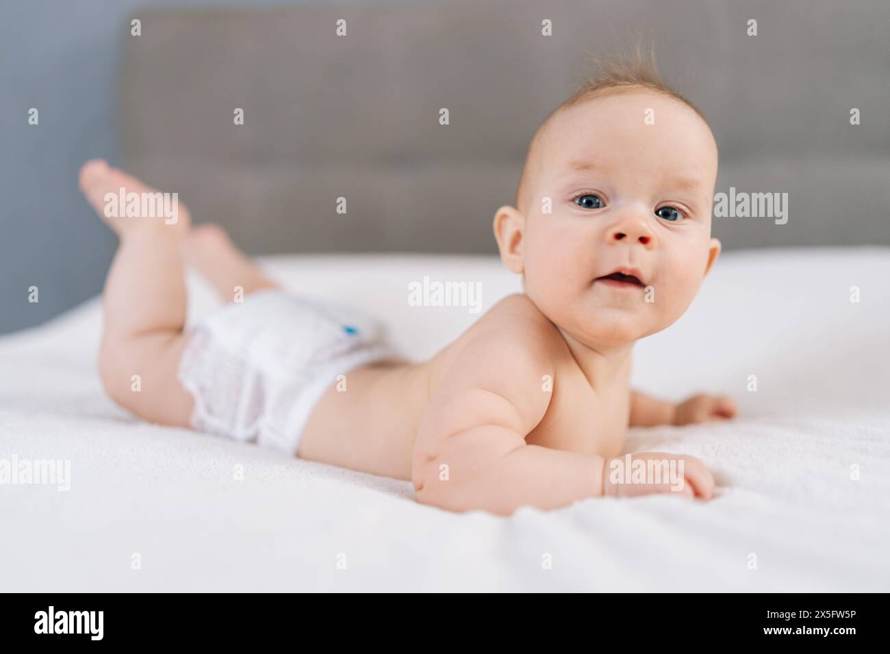 Portrait of cute healthy newborn baby lying in bed trying to crawl ...