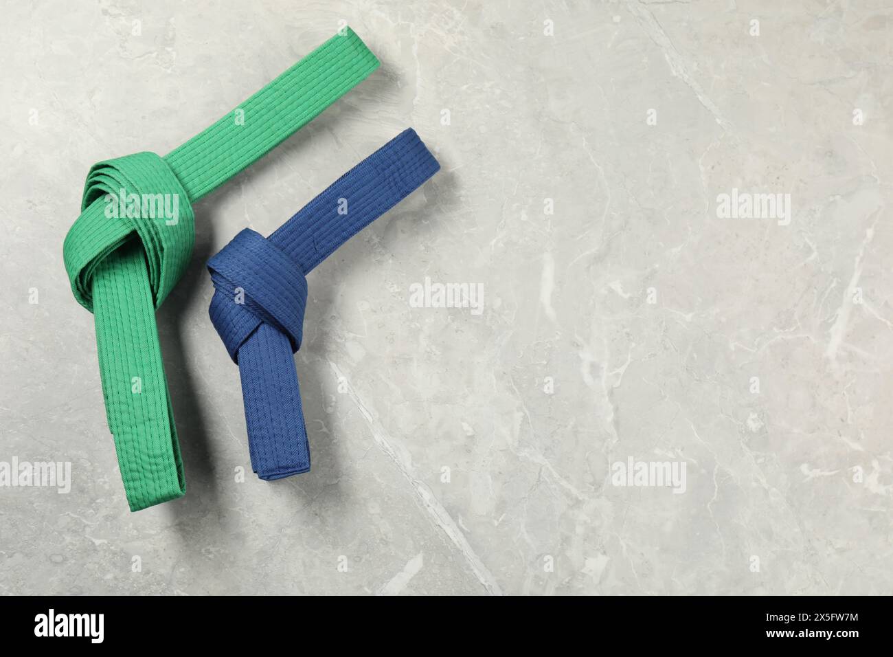 Green and blue karate belts on gray marble background, flat lay. Space ...