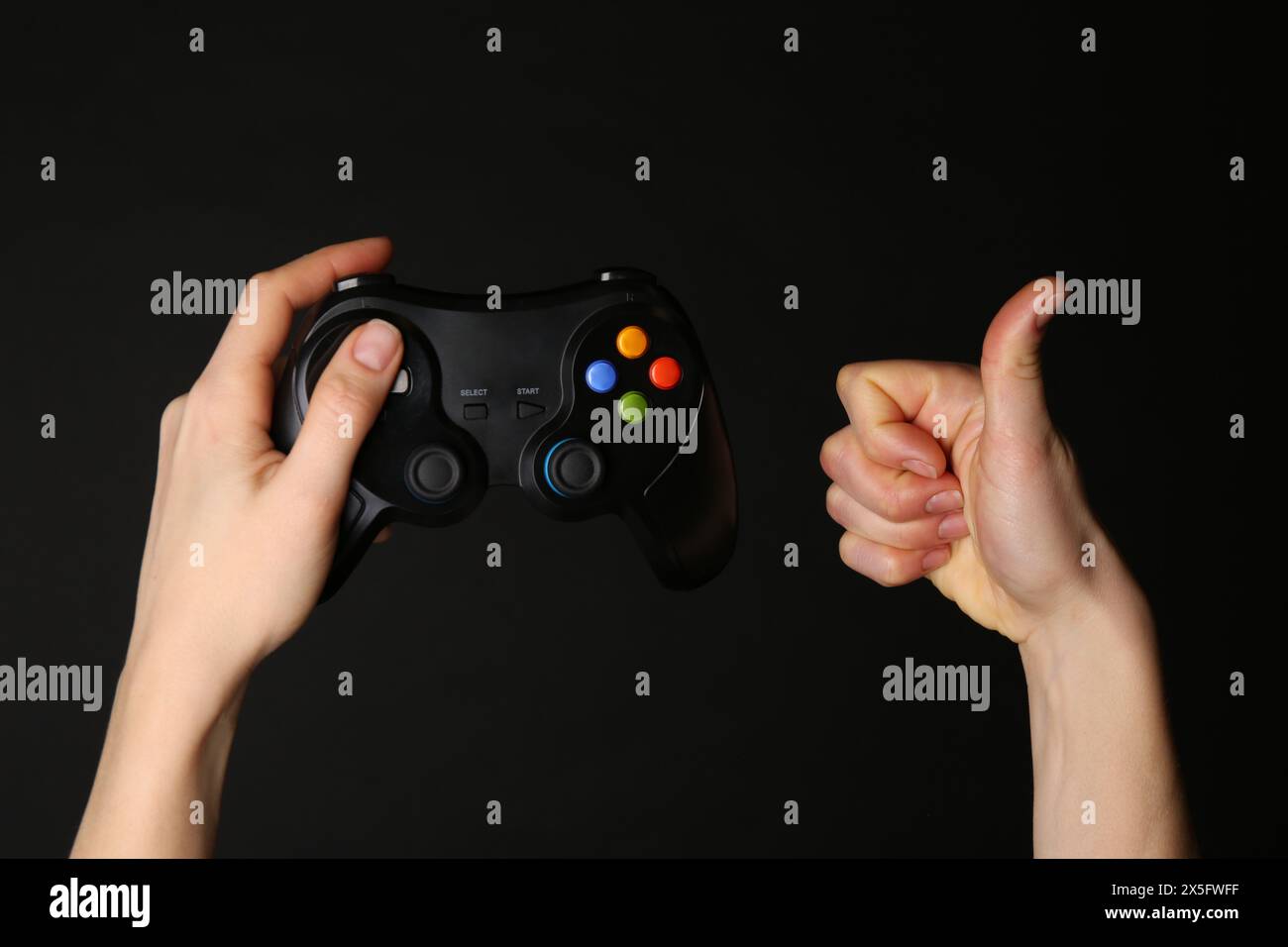 Woman with game controller showing thumbs up on black background ...
