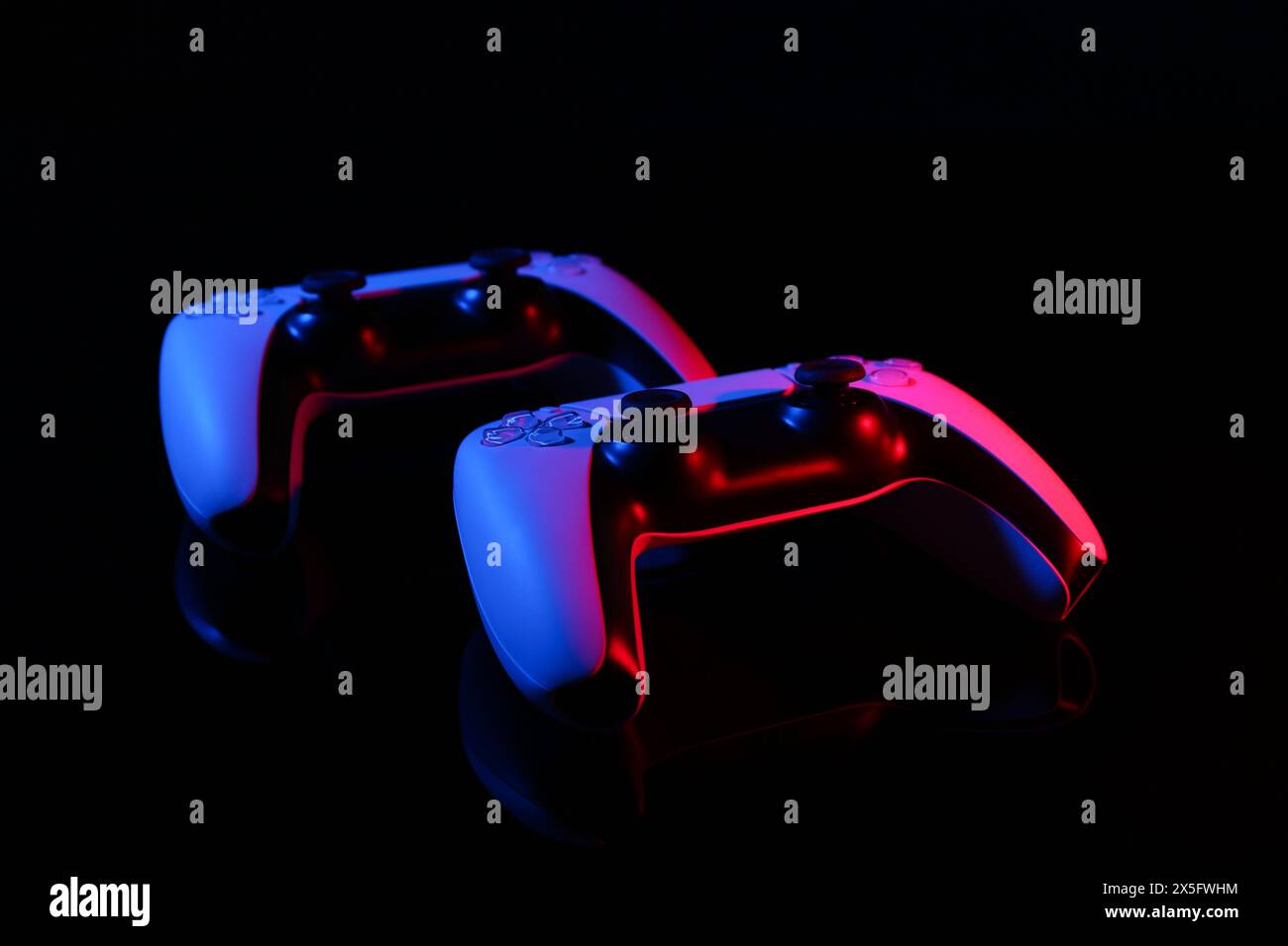 Wireless game controllers on black mirror surface in neon lights Stock ...