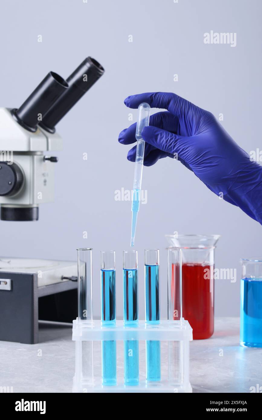 Scientist dripping liquid from pipette into test tube at grey marble ...