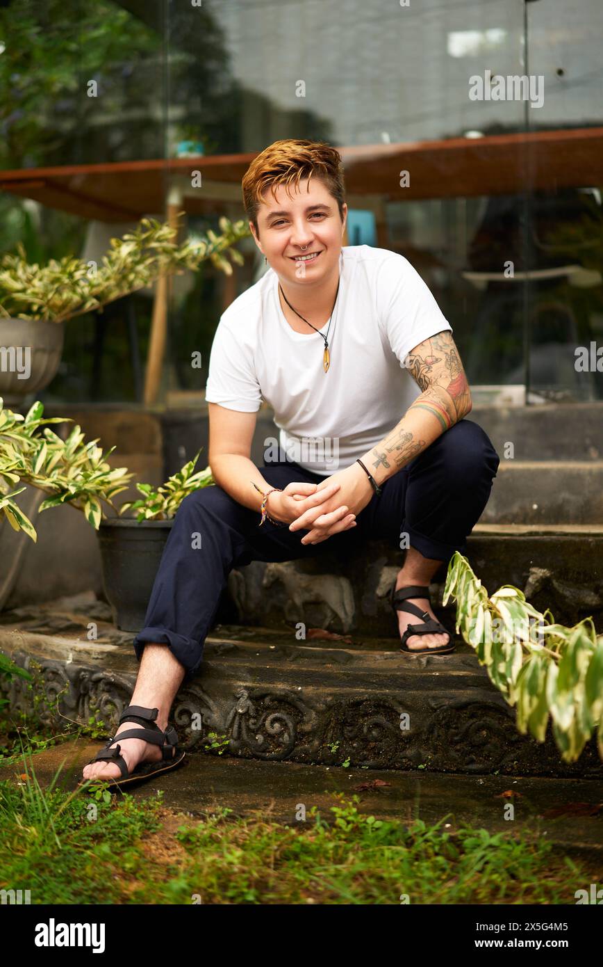 Gen Z Transgender man sits casually on stone steps, at modern coworking ...