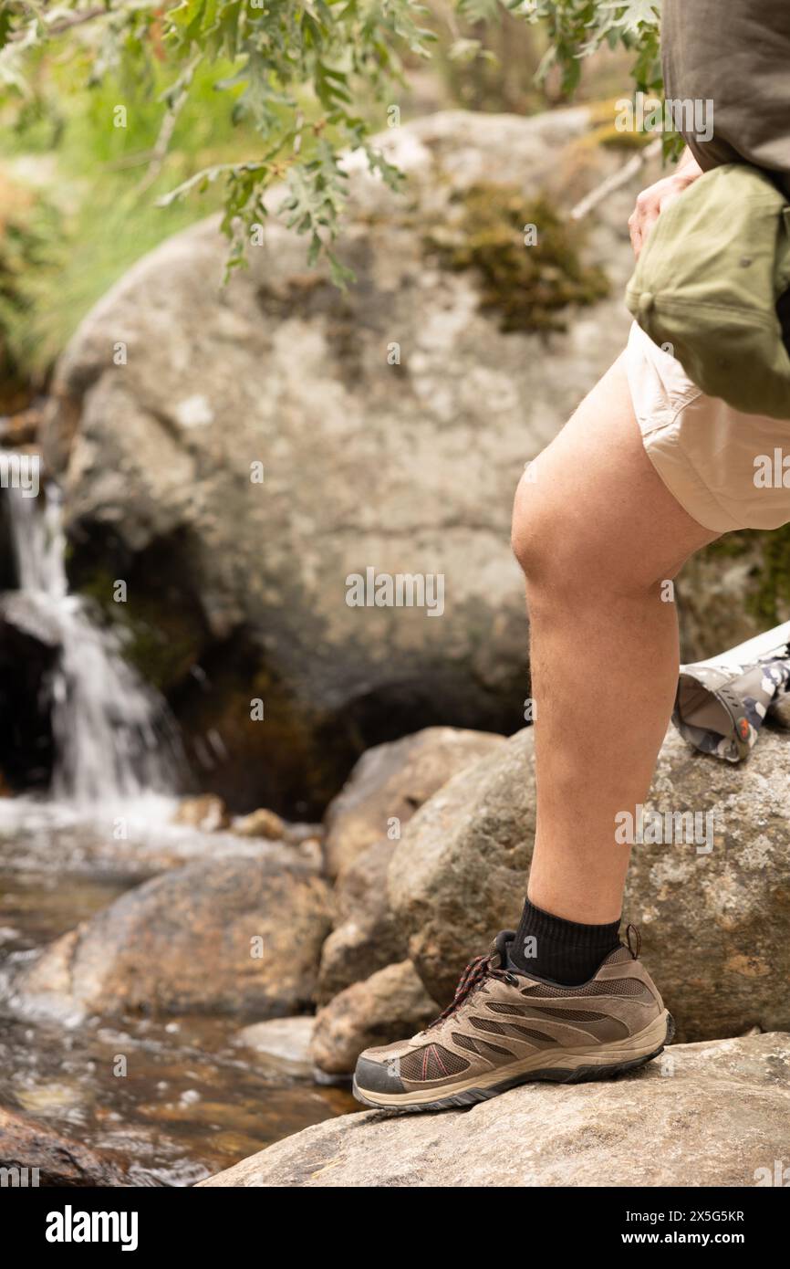 legs of man in hiking boots trekking over rocks with river and ...