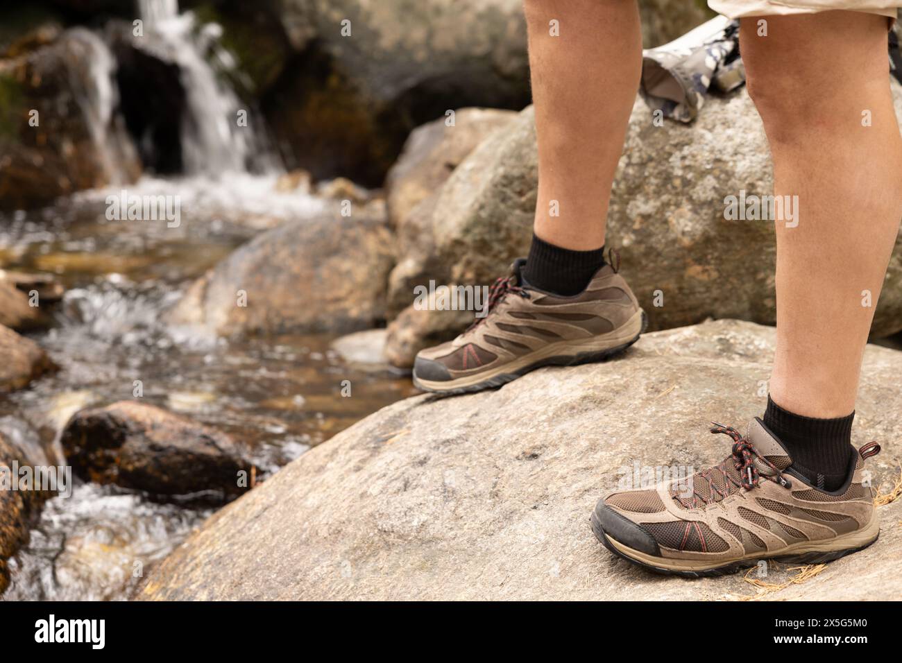 legs of man in hiking boots trekking over rocks with river and ...