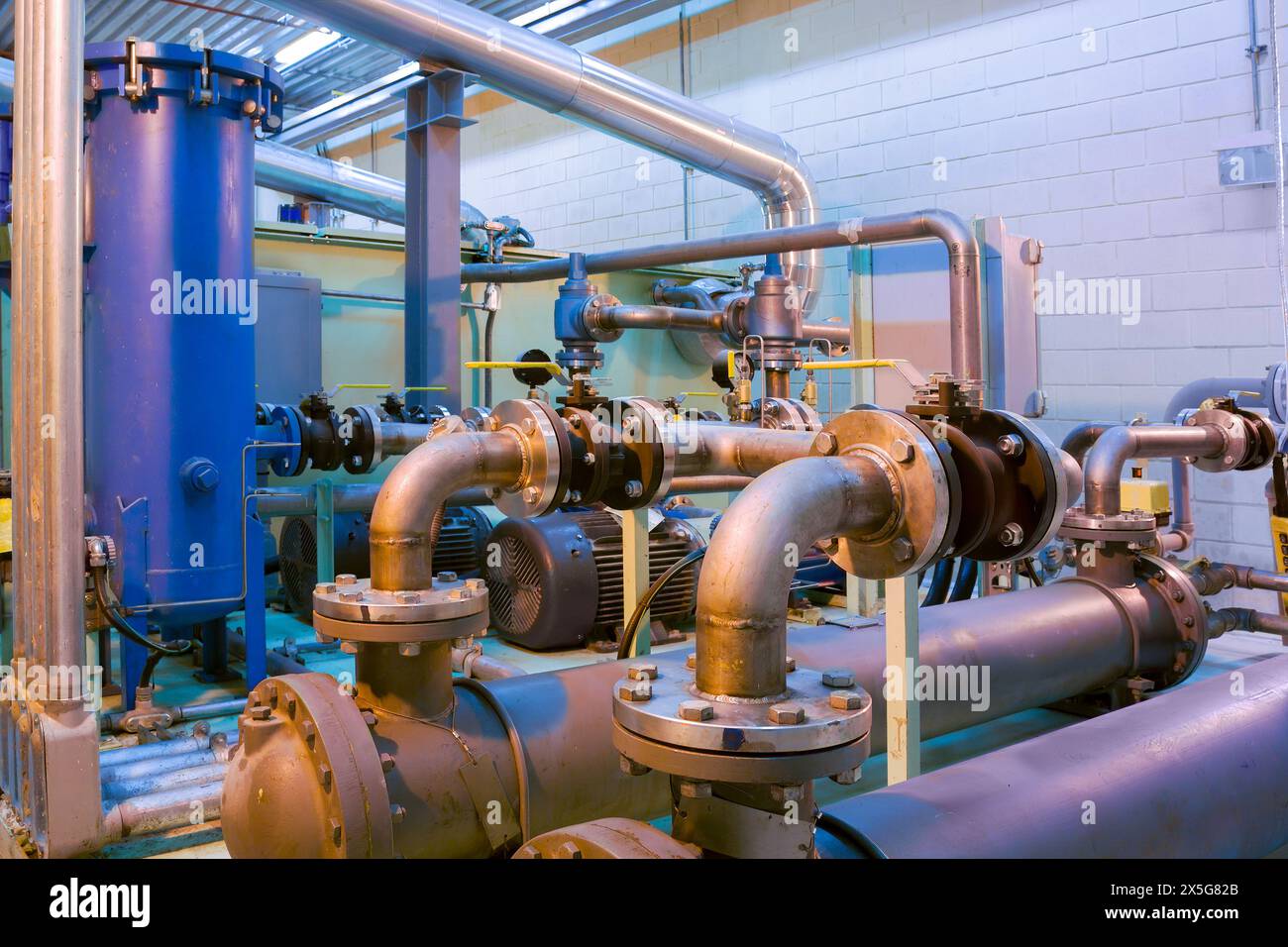 An array of metal pipes, valves, and pumps within an industrial plant ...