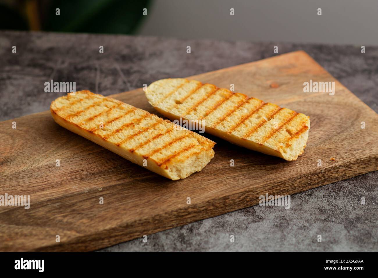 Two pieces of bread with grill marks on them are on a wooden cutting ...
