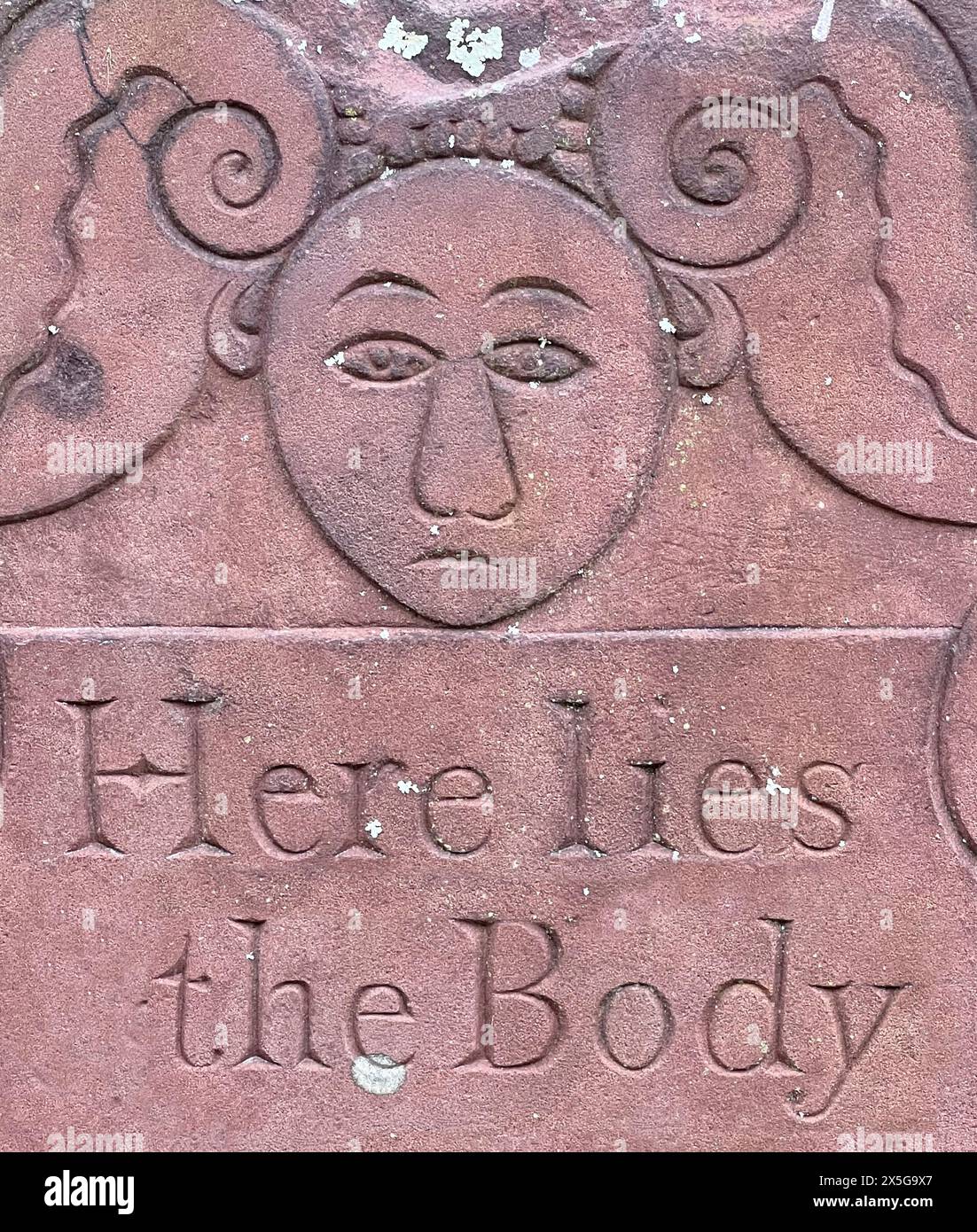A detailed relief carving of a cherubic face adorns an aged gravestone ...
