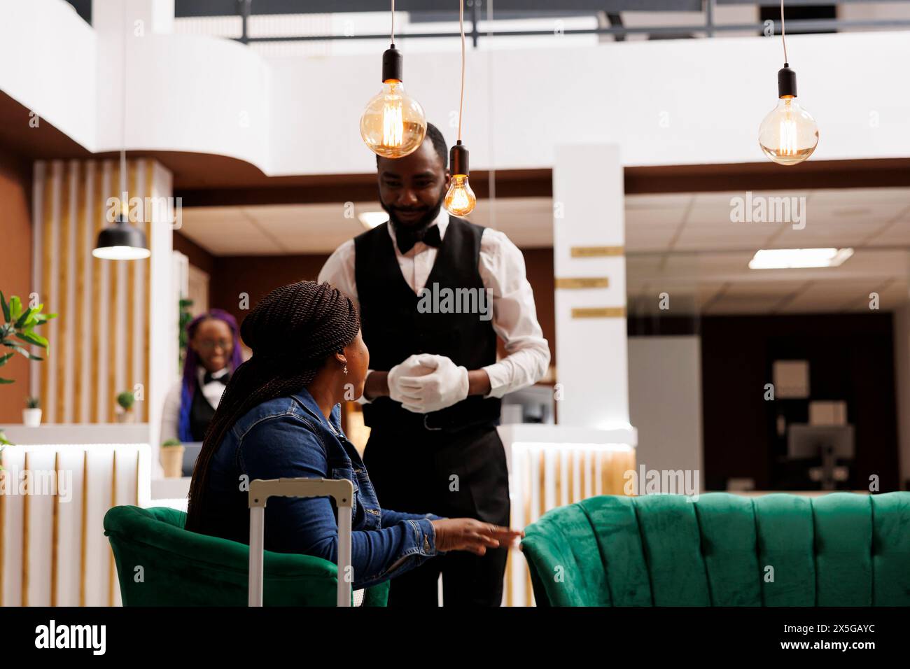 Smiling friendly hotel bellboy wearing uniform talking with African ...