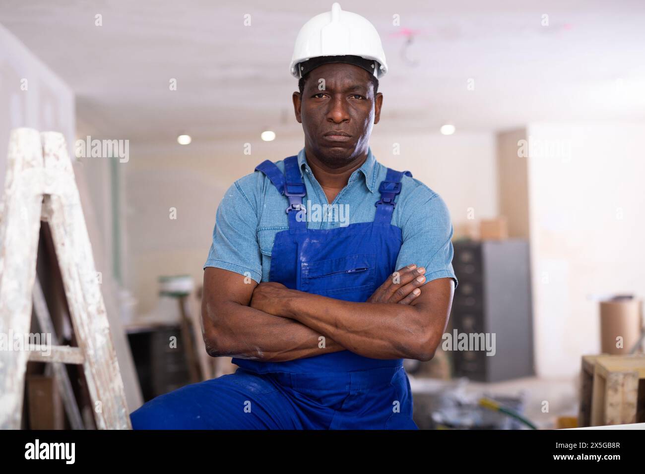 Portrait of confident african-american worker in blue overalls in room ...