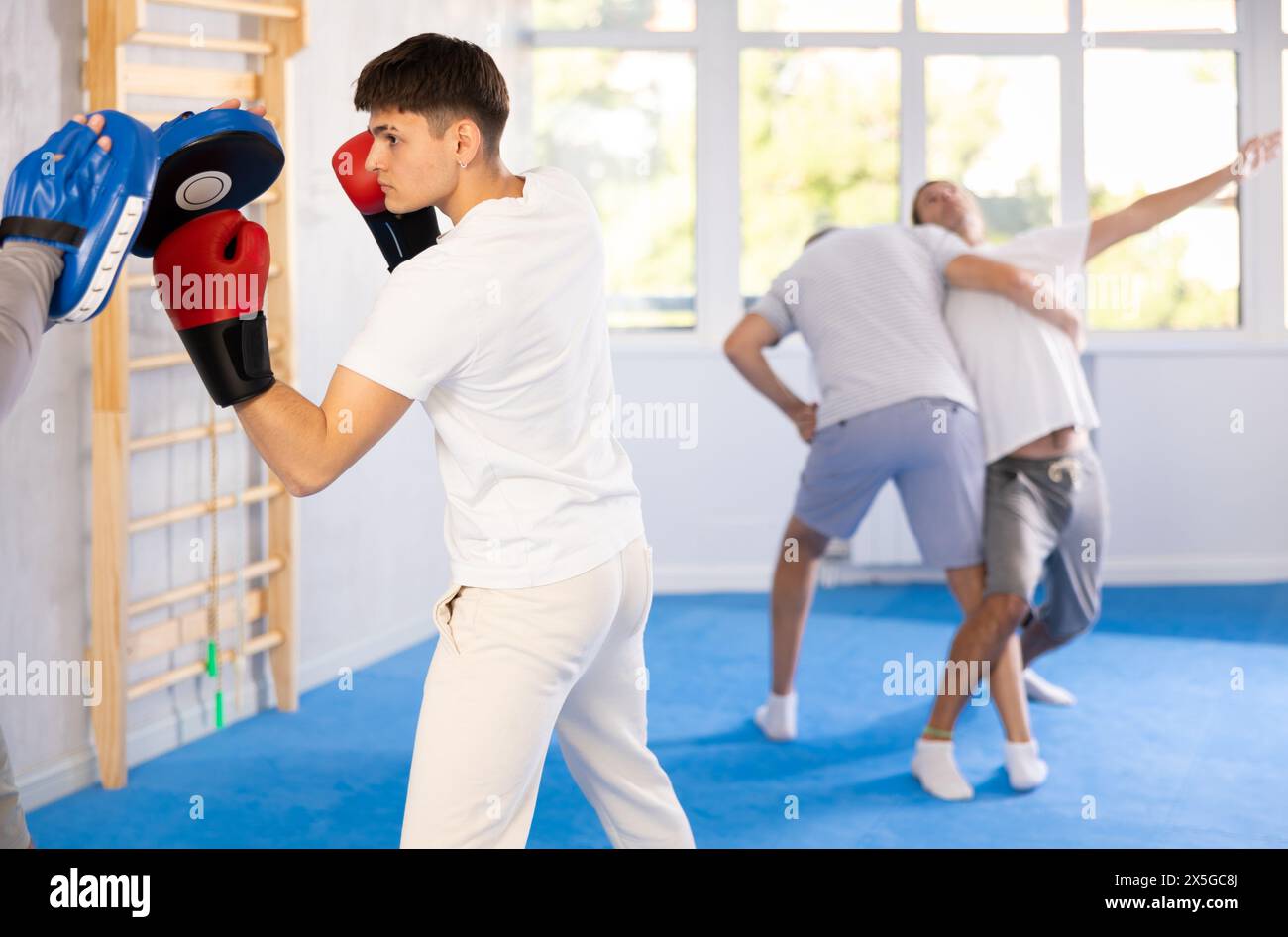 Coach holding mitts during self defence training in gym with young guy ...