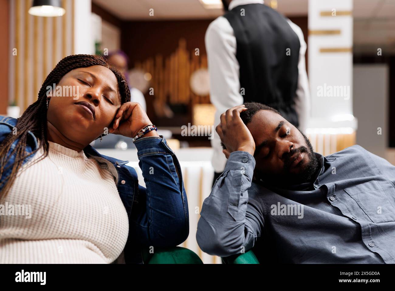 Young tired African American couple napping in hotel lobby, arriving ...