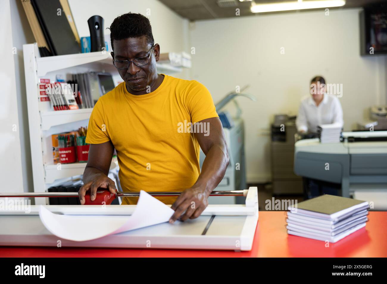 Concentrated African American male typographer using paper cutter on ...