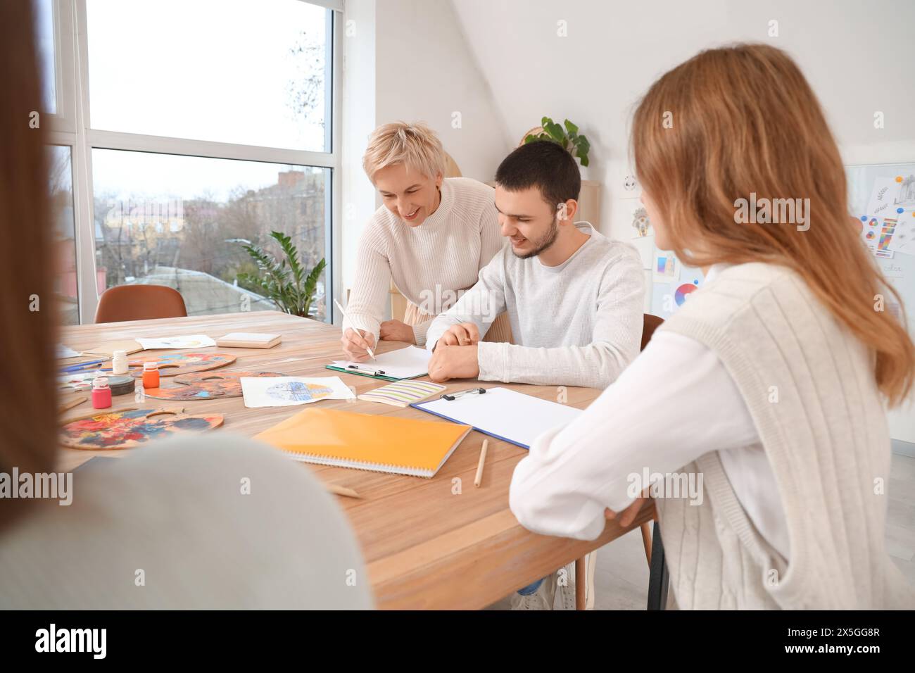 Mature art teacher helping student to draw during lecture at school ...