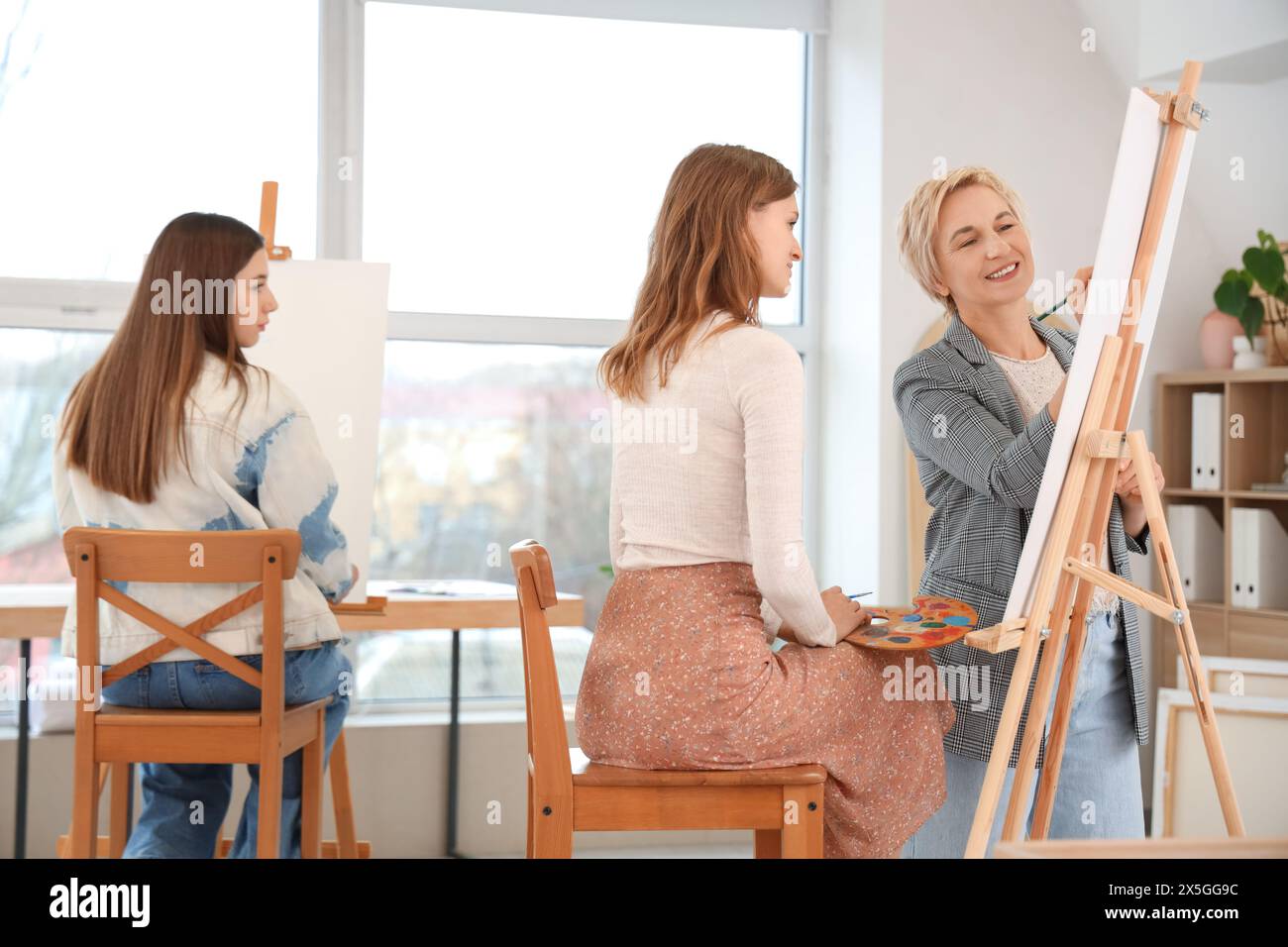 Female art teacher helping student to draw on canvas at school Stock ...