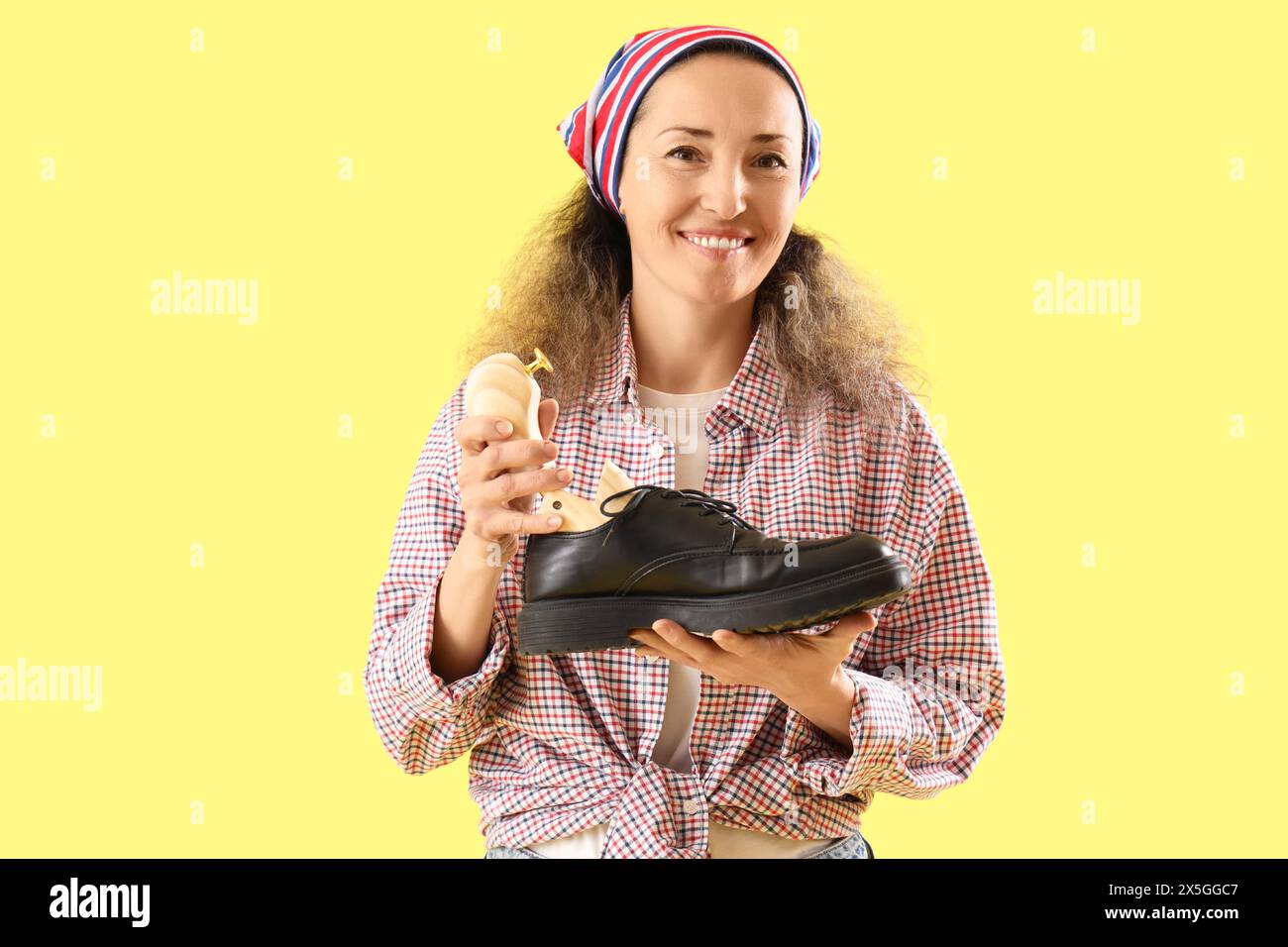 Female shoemaker with wooden shoe tree and boot on yellow background ...