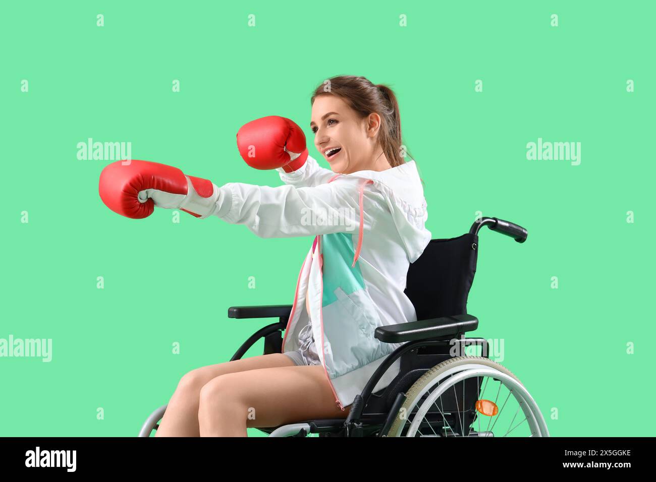 Sporty young woman in wheelchair with boxing gloves on green background ...
