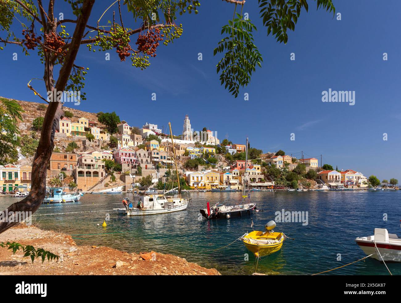 Hillside view of the colorful buildings and busy harbor on Symi Island ...