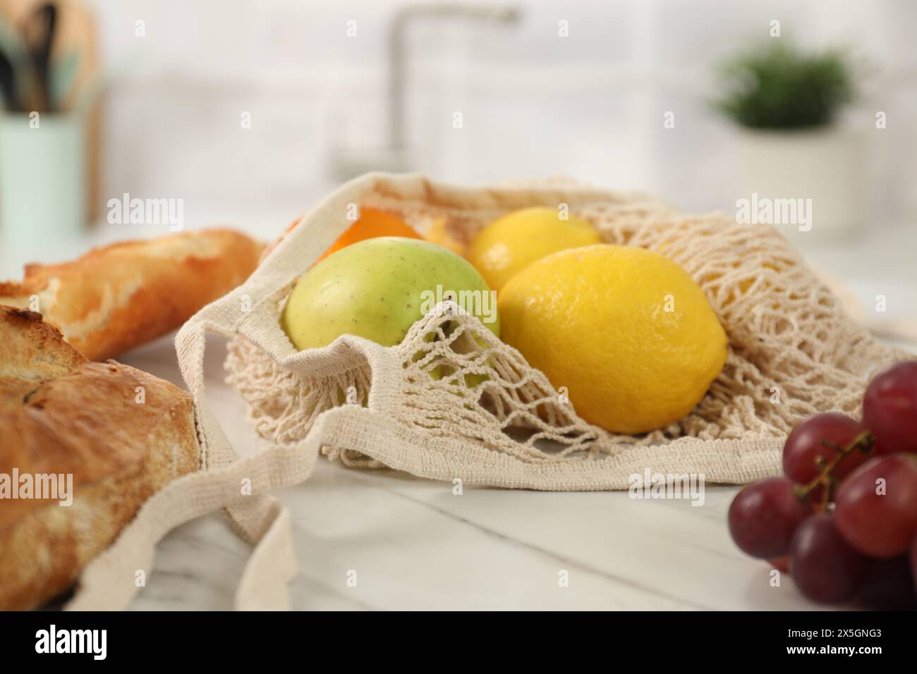 String bag with fresh fruits and baguettes on light table, closeup ...