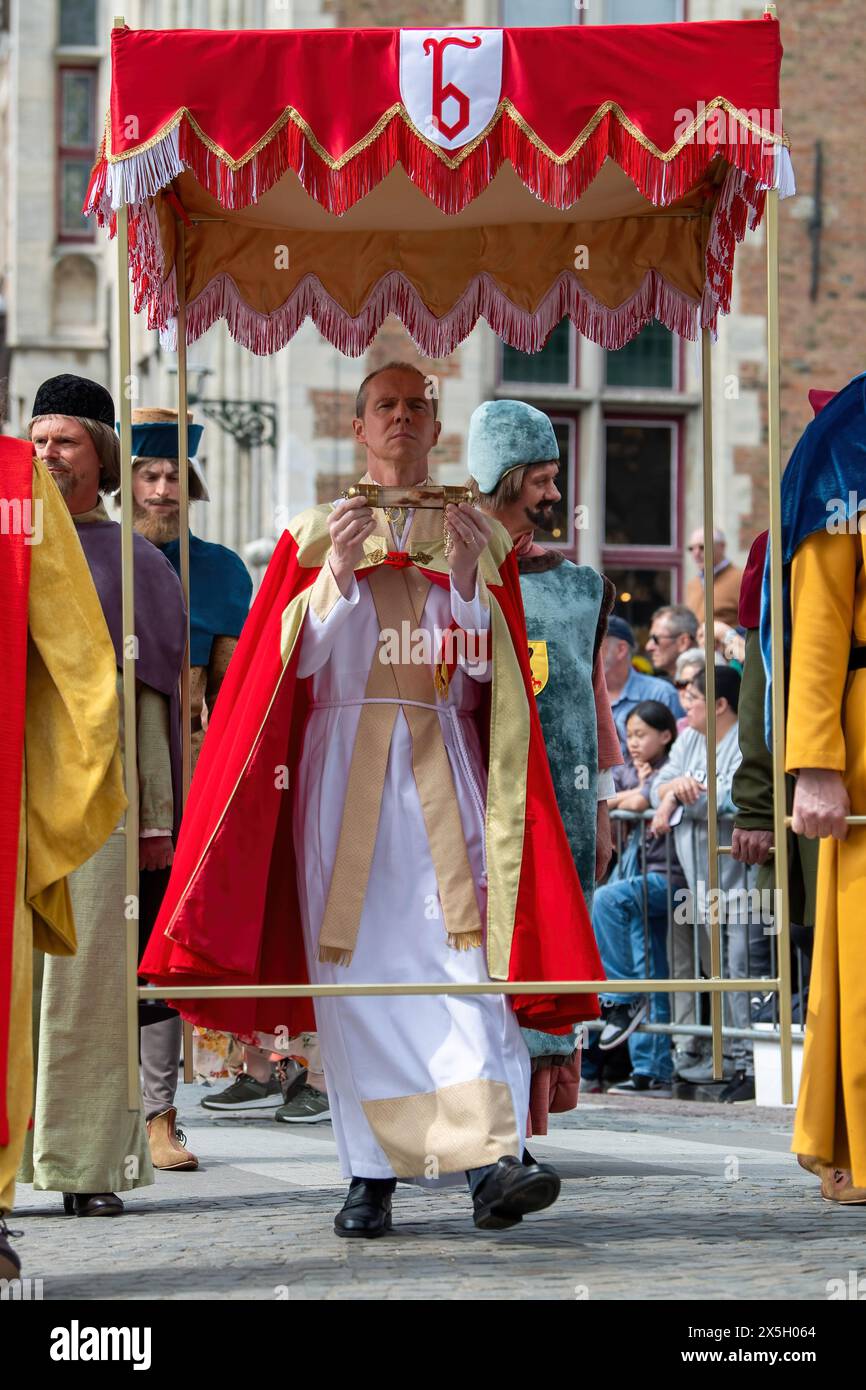 A priest carries the glass container that hold a piece of cloth that is ...