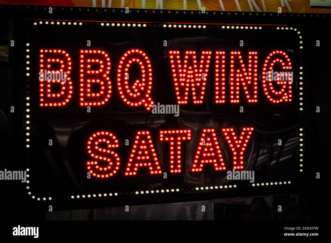 Brightly illuminated neon sign displaying 'BBQ Wing Satay' in red ...