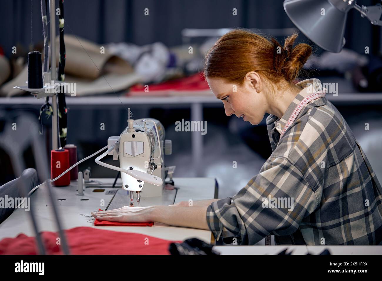 seamstress lady in casual wear sit behind table using sewing machine ...