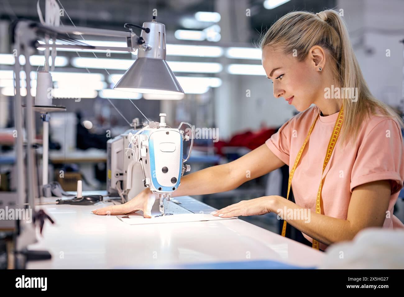 Nice Caucaian Blonde Textile Factory Worker On Production Line Using Modern Sewing Machine At