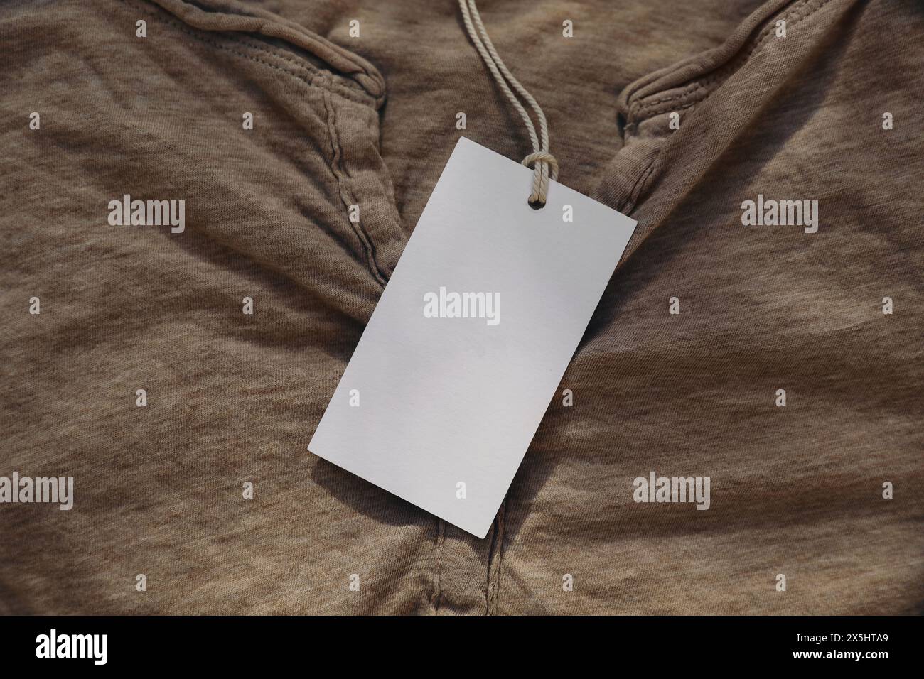 Price tag with rope hanging on folded beige cotton t-shirt. Closeup of ...