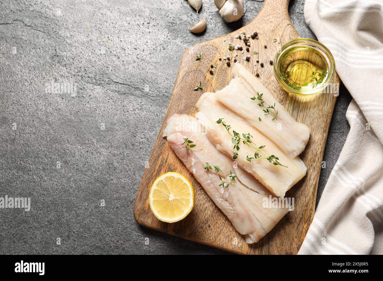 Raw cod fish, microgreens, oil, spices and lemon on grey textured table ...