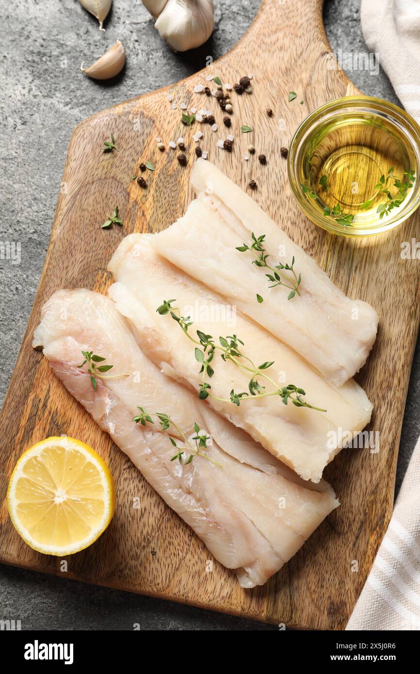 Raw cod fish, microgreens, oil, spices and lemon on grey textured table ...