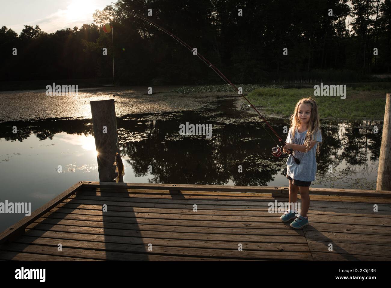 Cute little girl holding fishing pole with fish on dock Stock Photo - Alamy