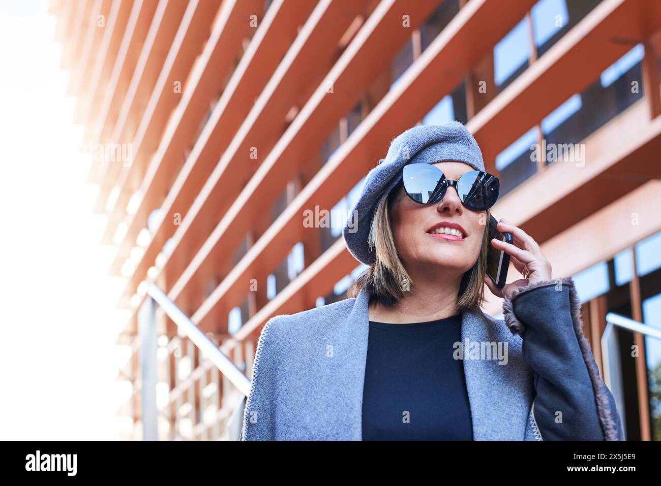 Stylish woman in conversation on phone, city backdrop Stock Photo - Alamy
