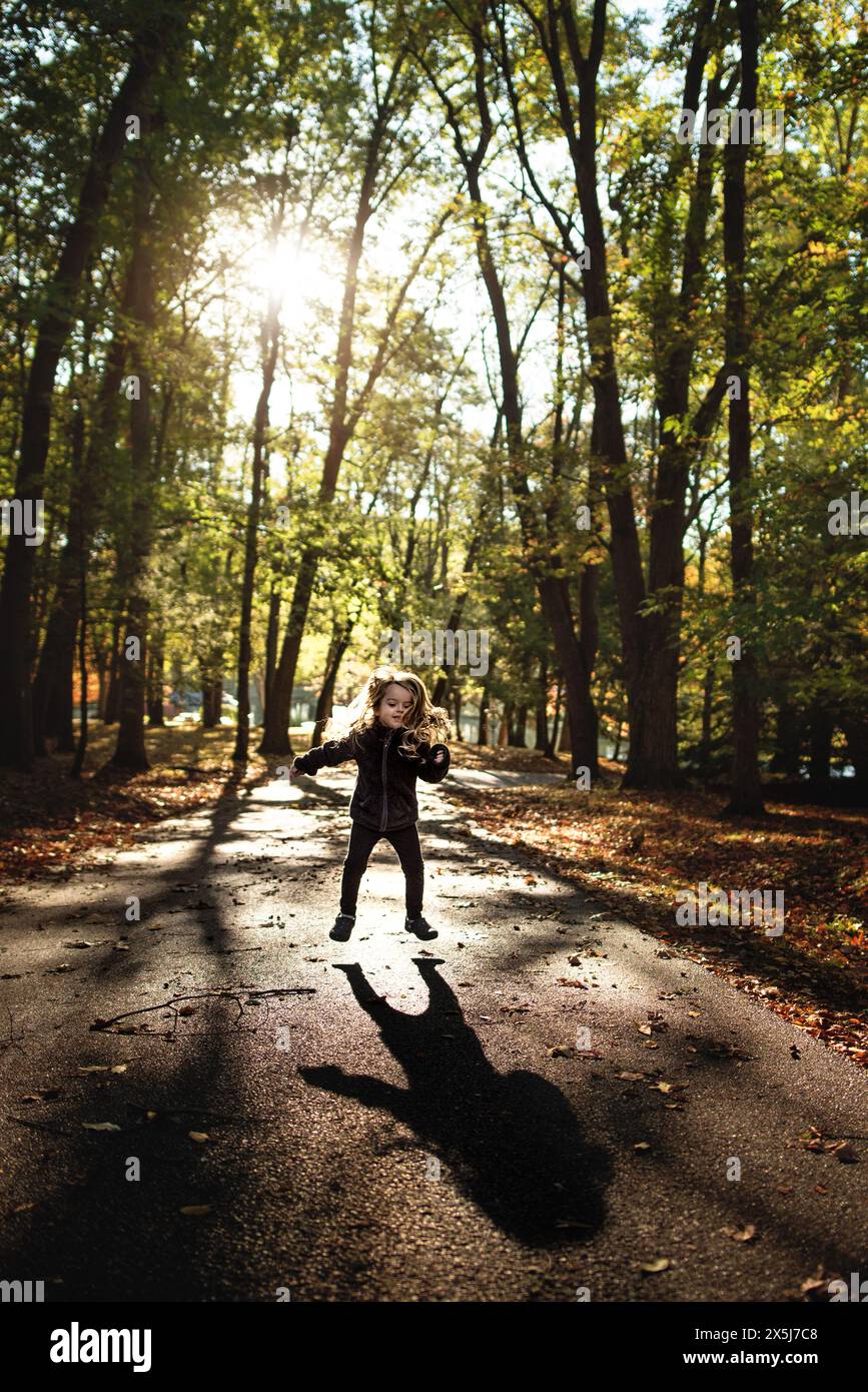 Little girl hopping down path in green forest on sunny day Stock Photo ...
