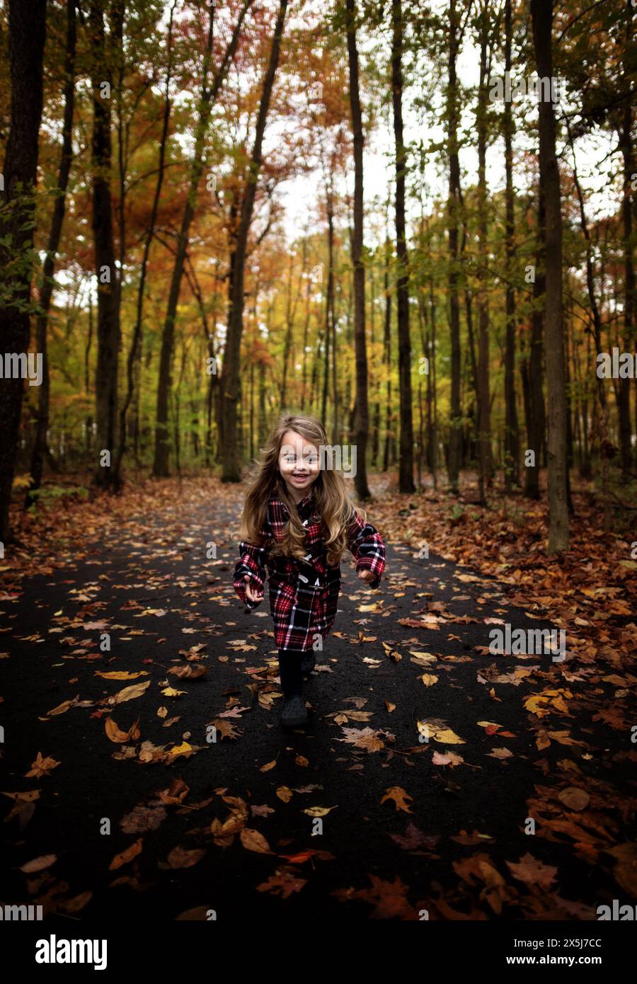 Happy young girl running down path with colorful leaves and trees Stock ...