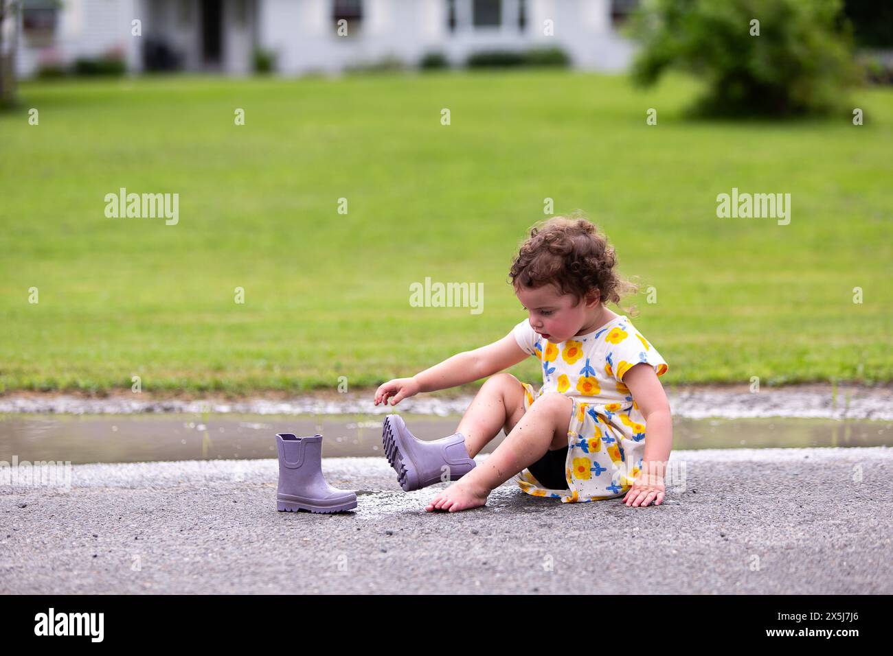 Toddler girl sitting and taking off rainboots Stock Photo - Alamy