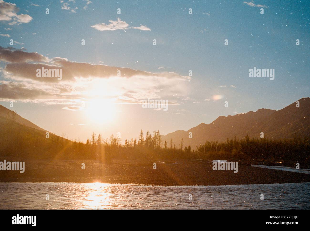 The sun peaks through the sky overlooking an Alaska River Stock Photo ...