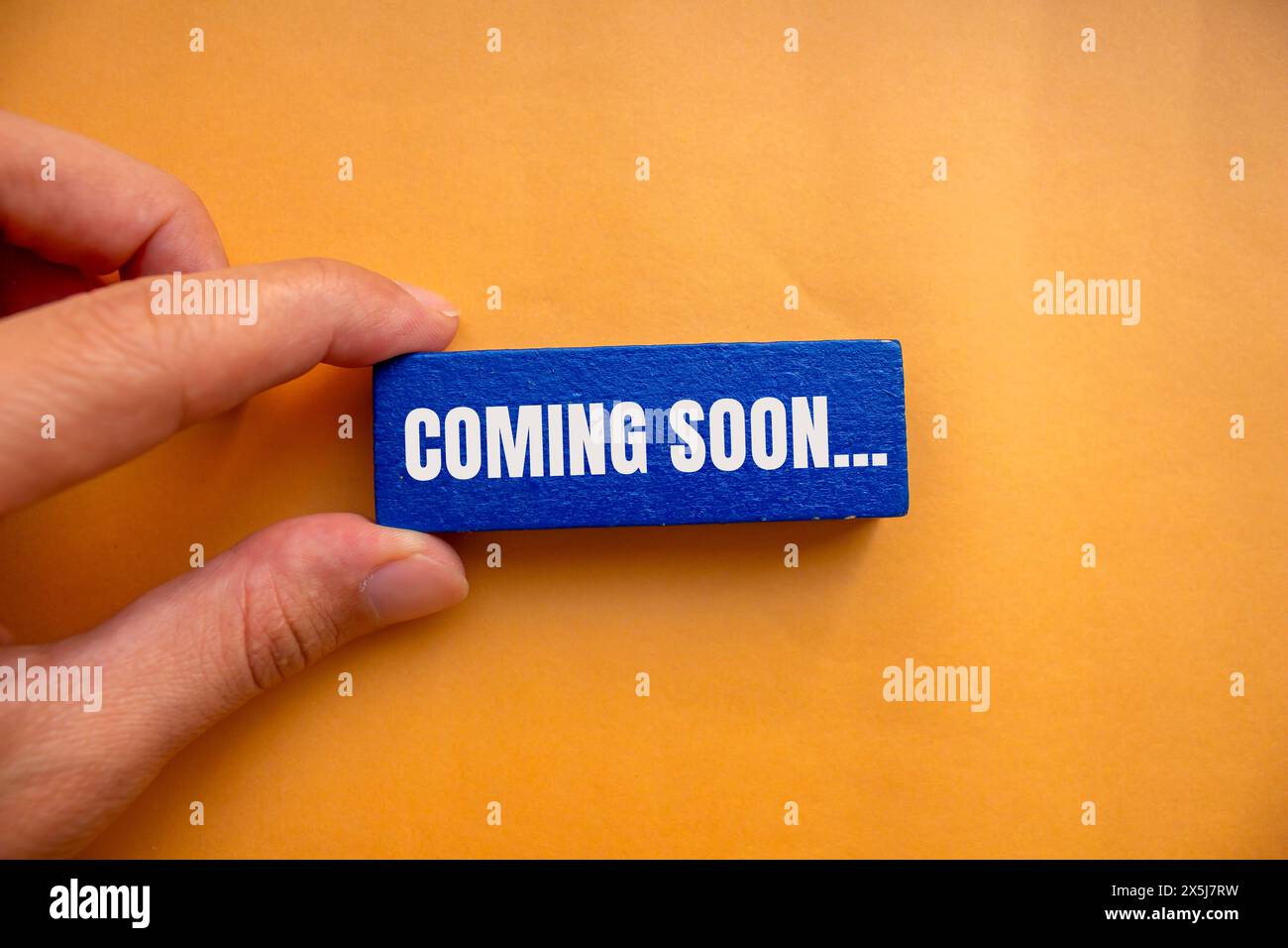 Coming soon words written on blue wooden block with orange background ...