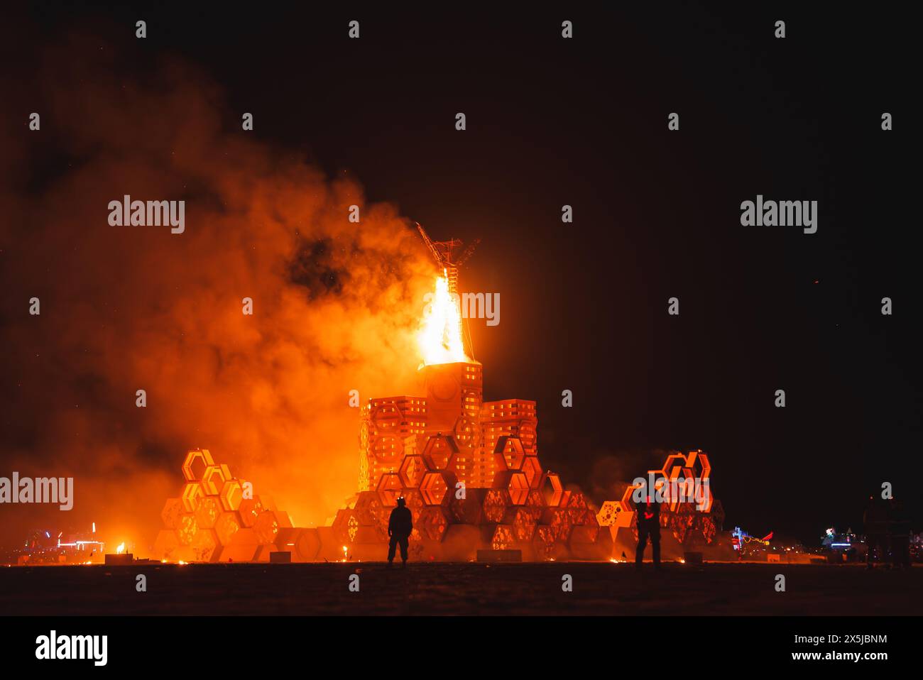Night scene at desert festival elaborate structure ablaze, spectators ...
