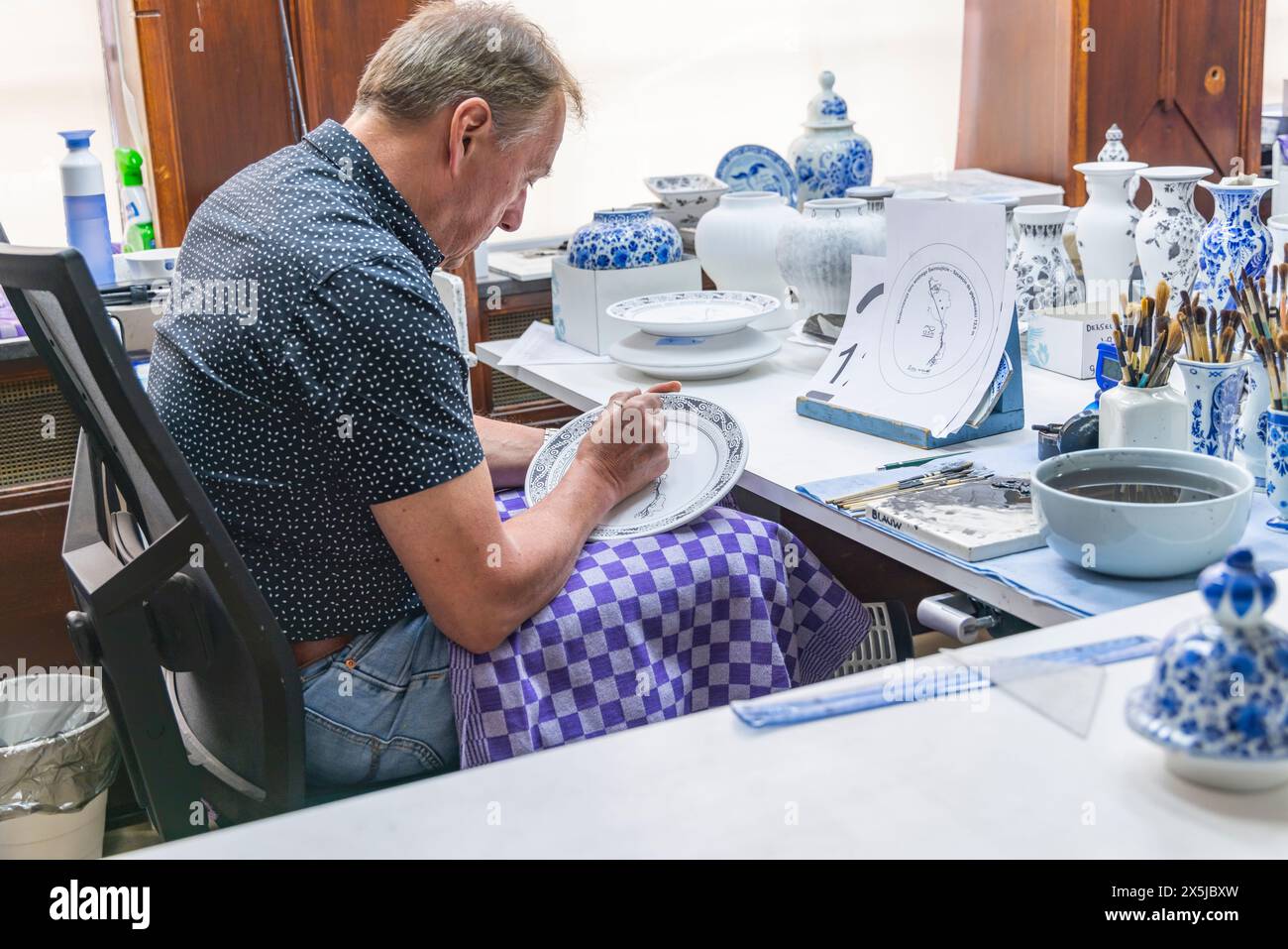 Netherlands, South Holland, Delft. Artisan painting glaze onto plates ...