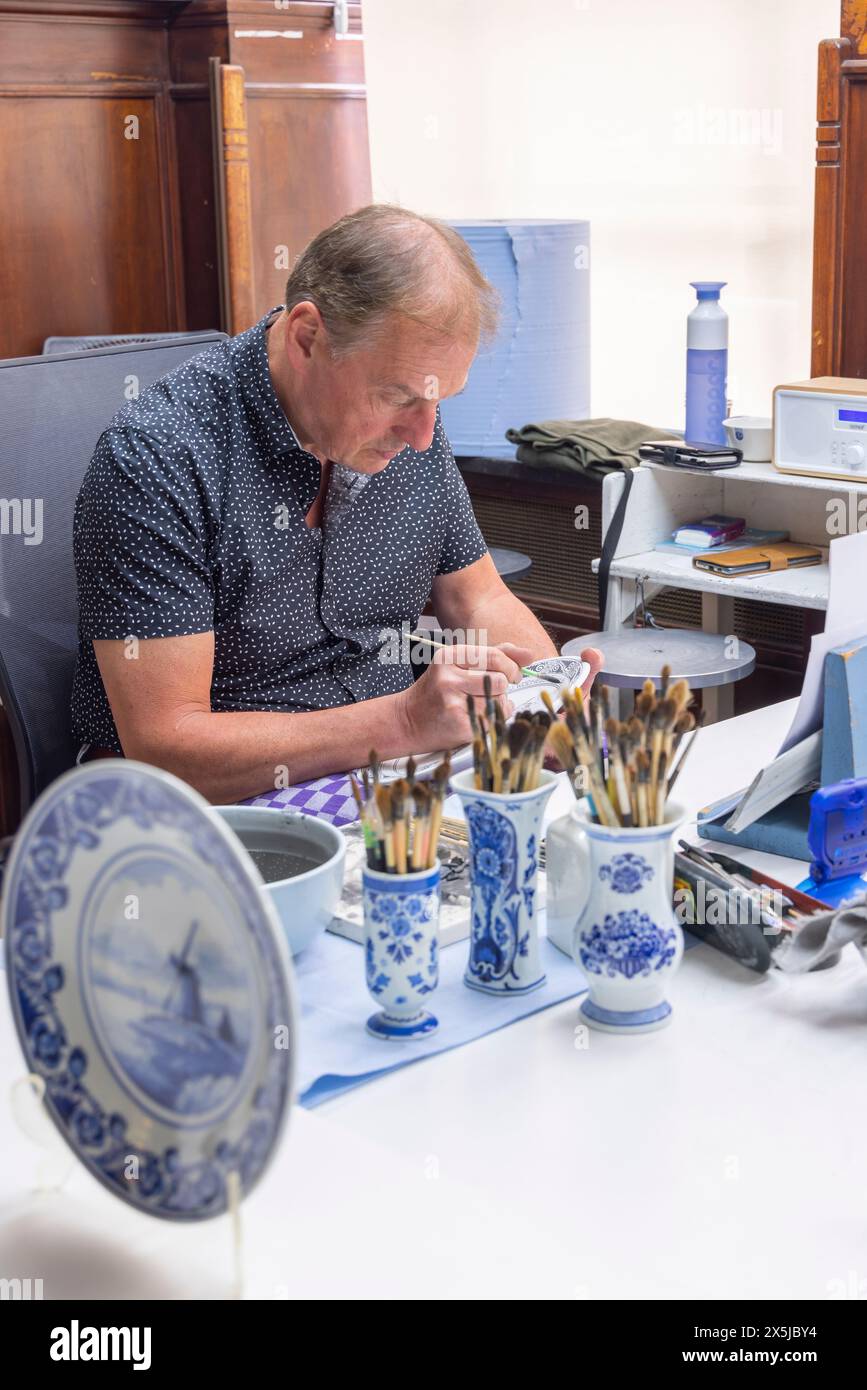 Netherlands, South Holland, Delft. Artisan painting glaze onto plates ...
