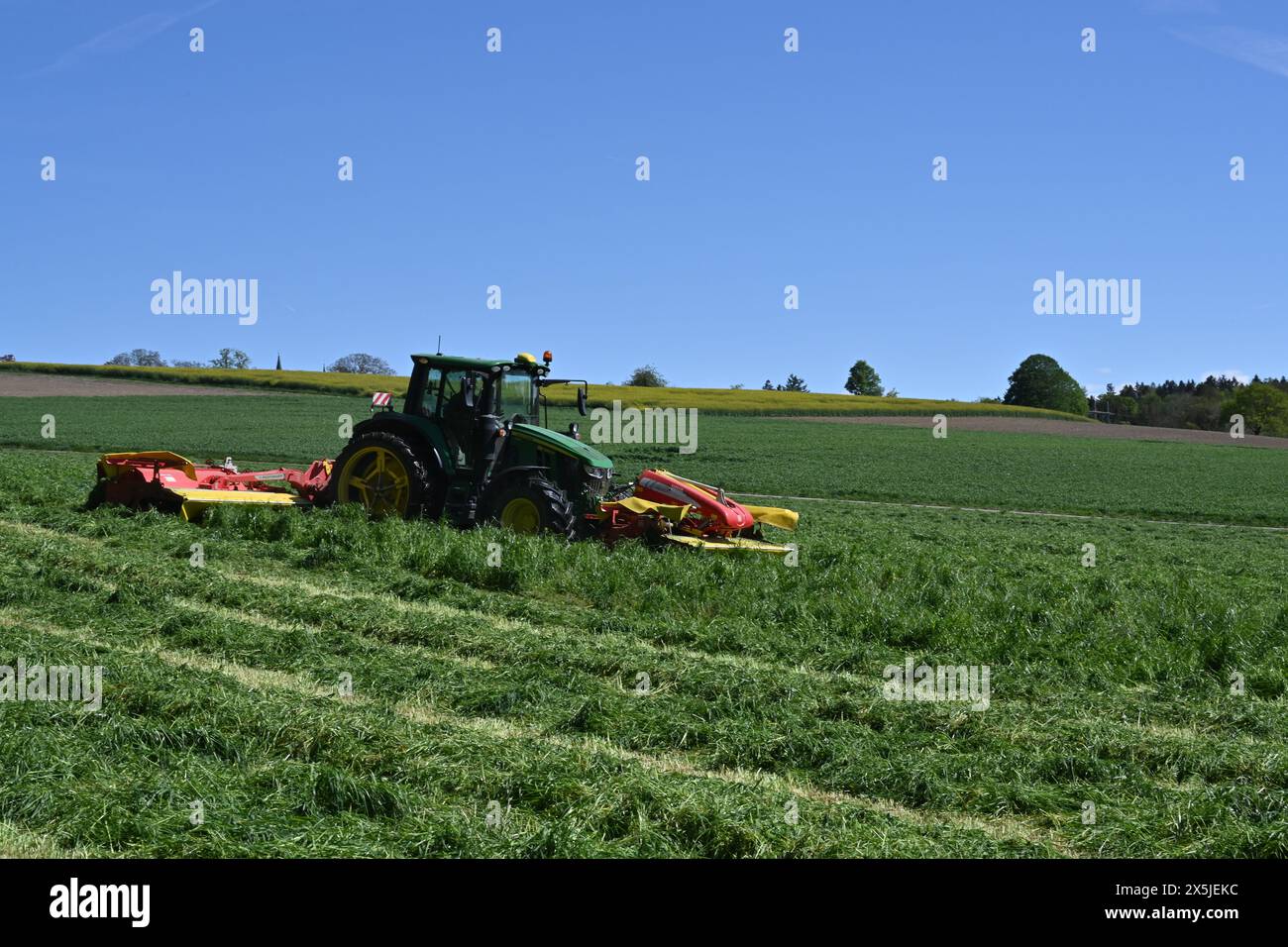 Green tractor with grass mowing mechanism captured during spring mowing ...