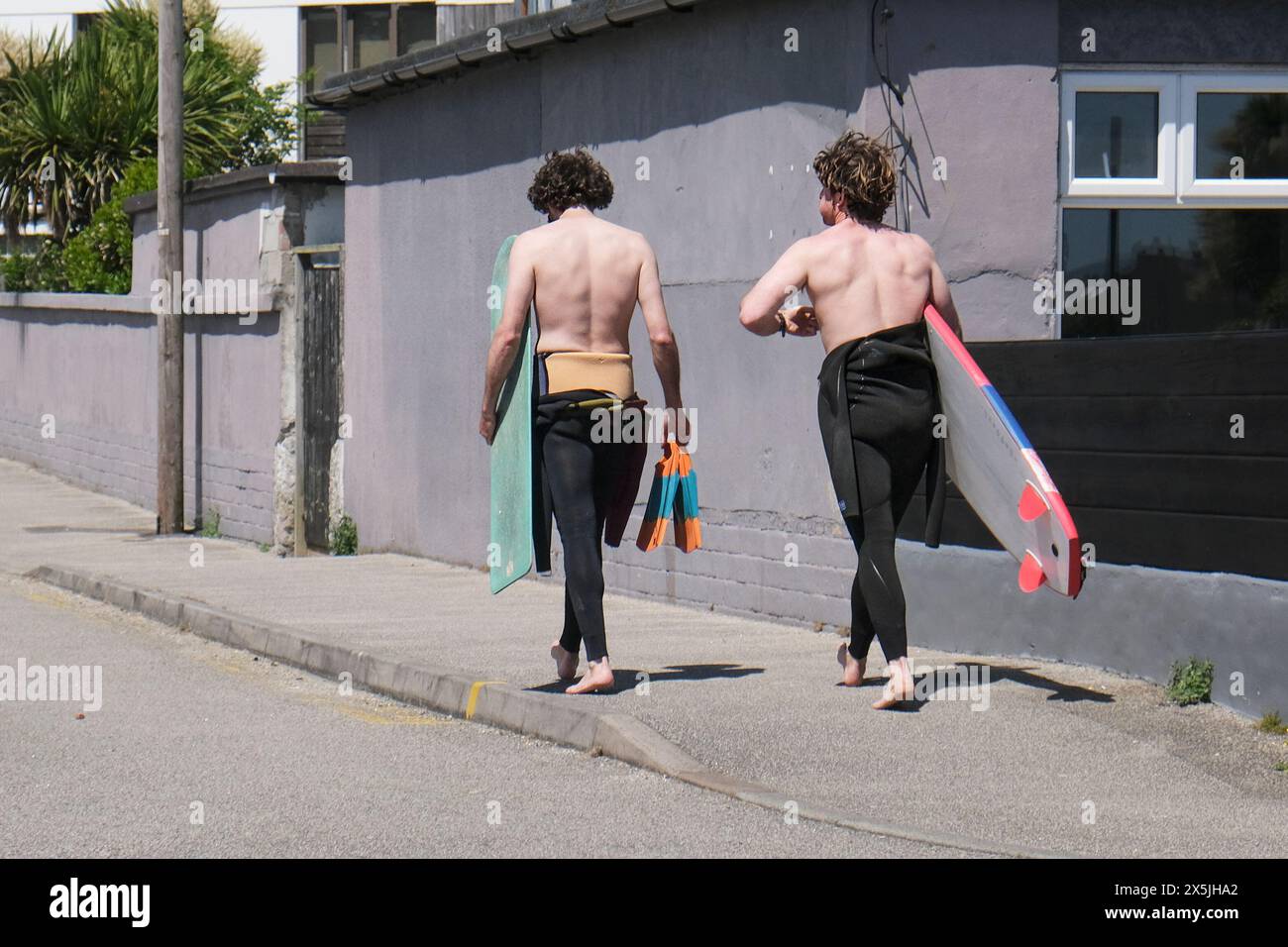 Two male surfers carrying their surfboards along a street after surfing ...