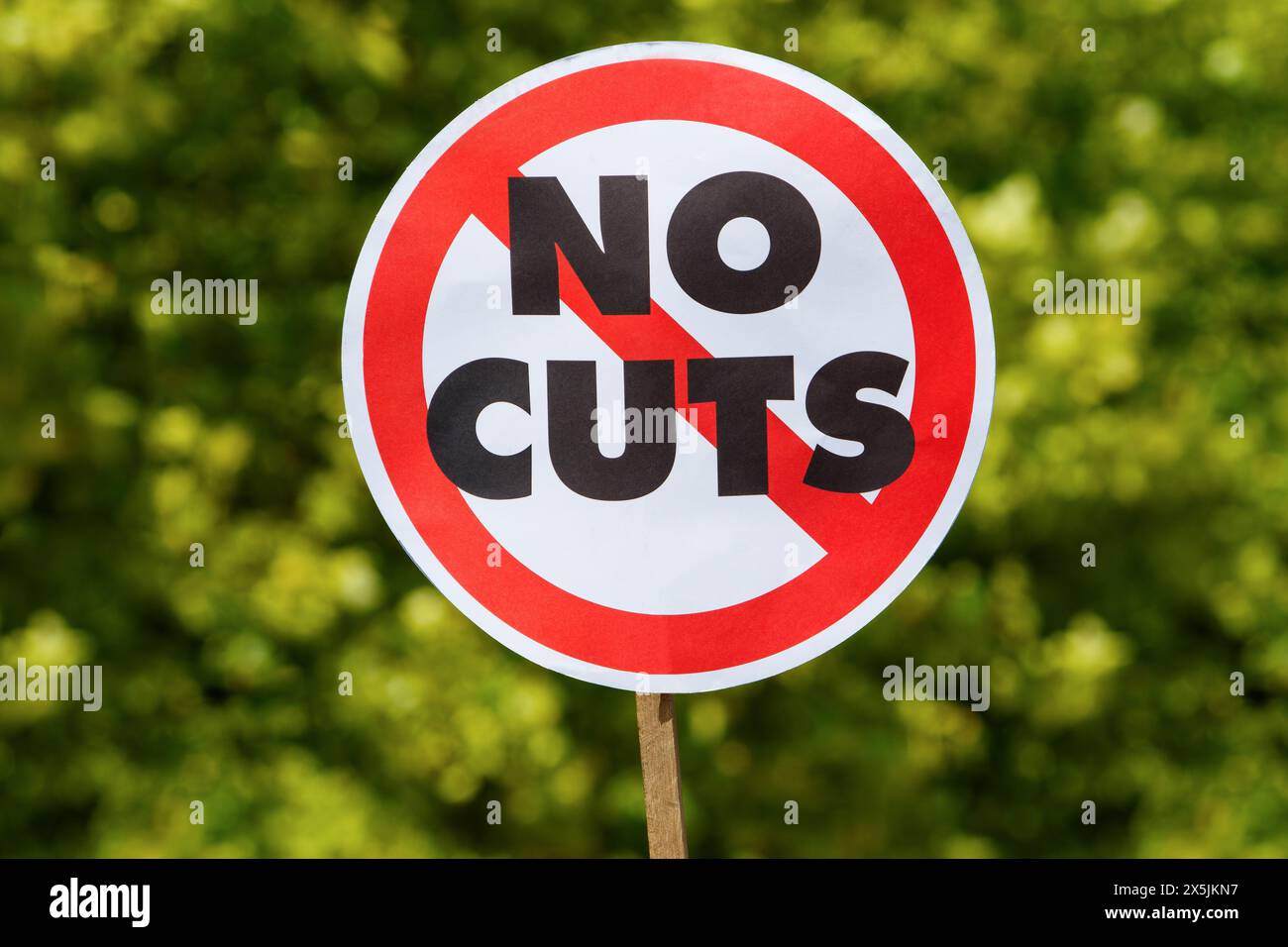 A round protest placard styled like a UK road sign with "No Cuts ...