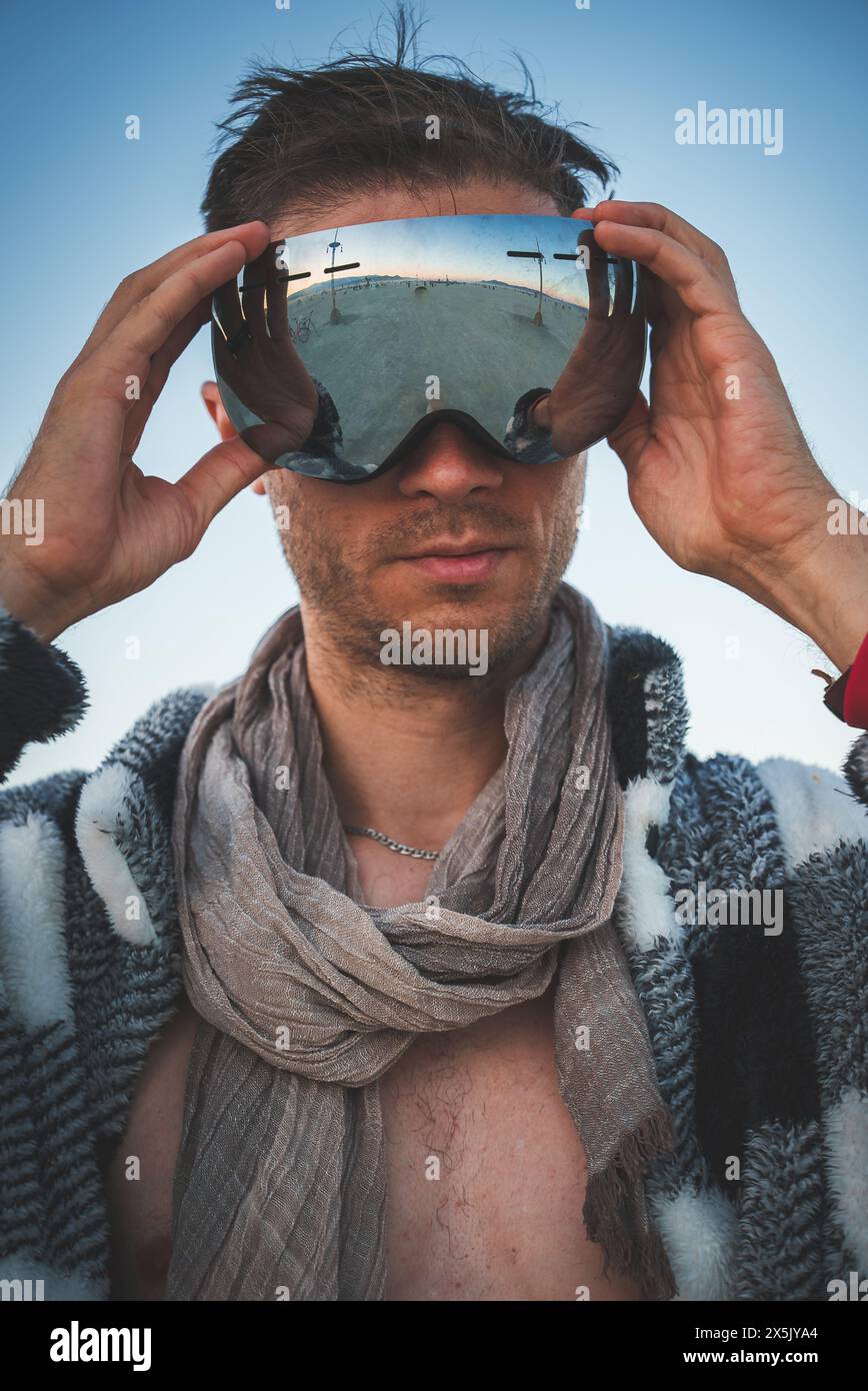 Young man in desert setting adjusting goggles, festival attire ...