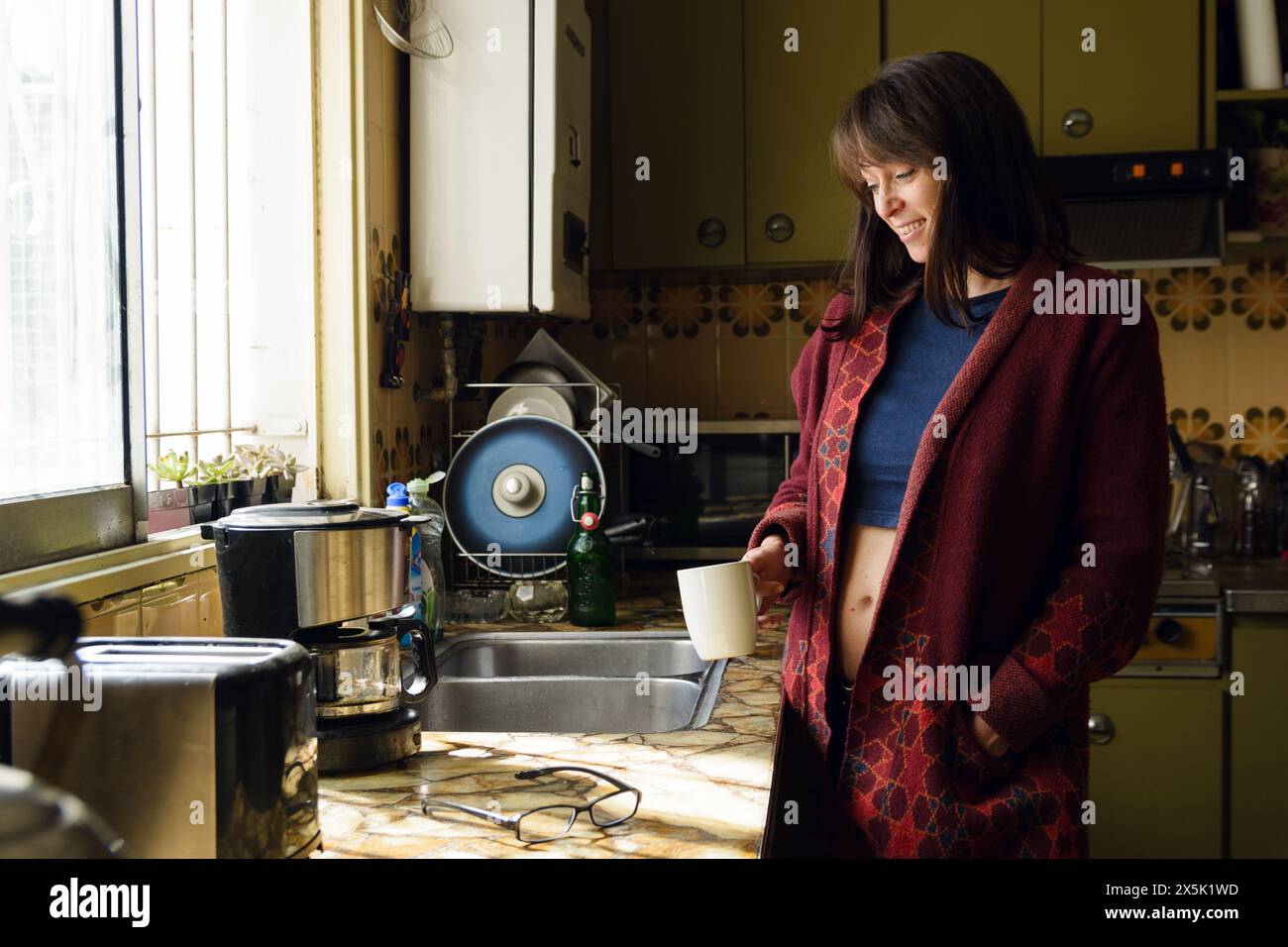A Latin adult Woman wearing red sweater standing in Kitchen of her home ...