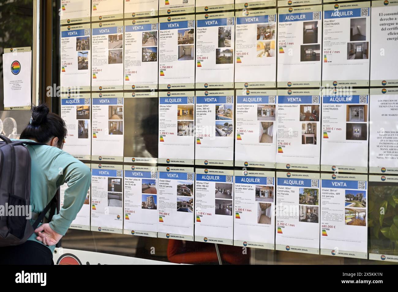 Person looking at listing of properties in estate agents window display ...