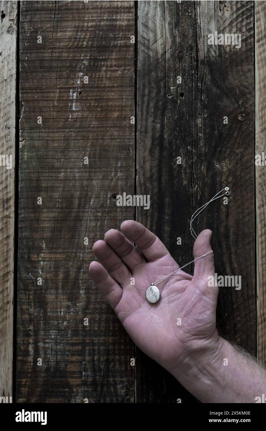 A mans open hand laying on old wood background with silver locket ...