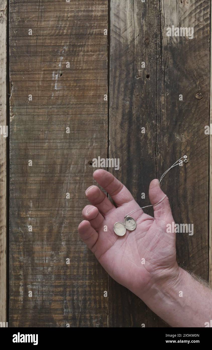 A mans open hand laying on old wood background with silver locket ...