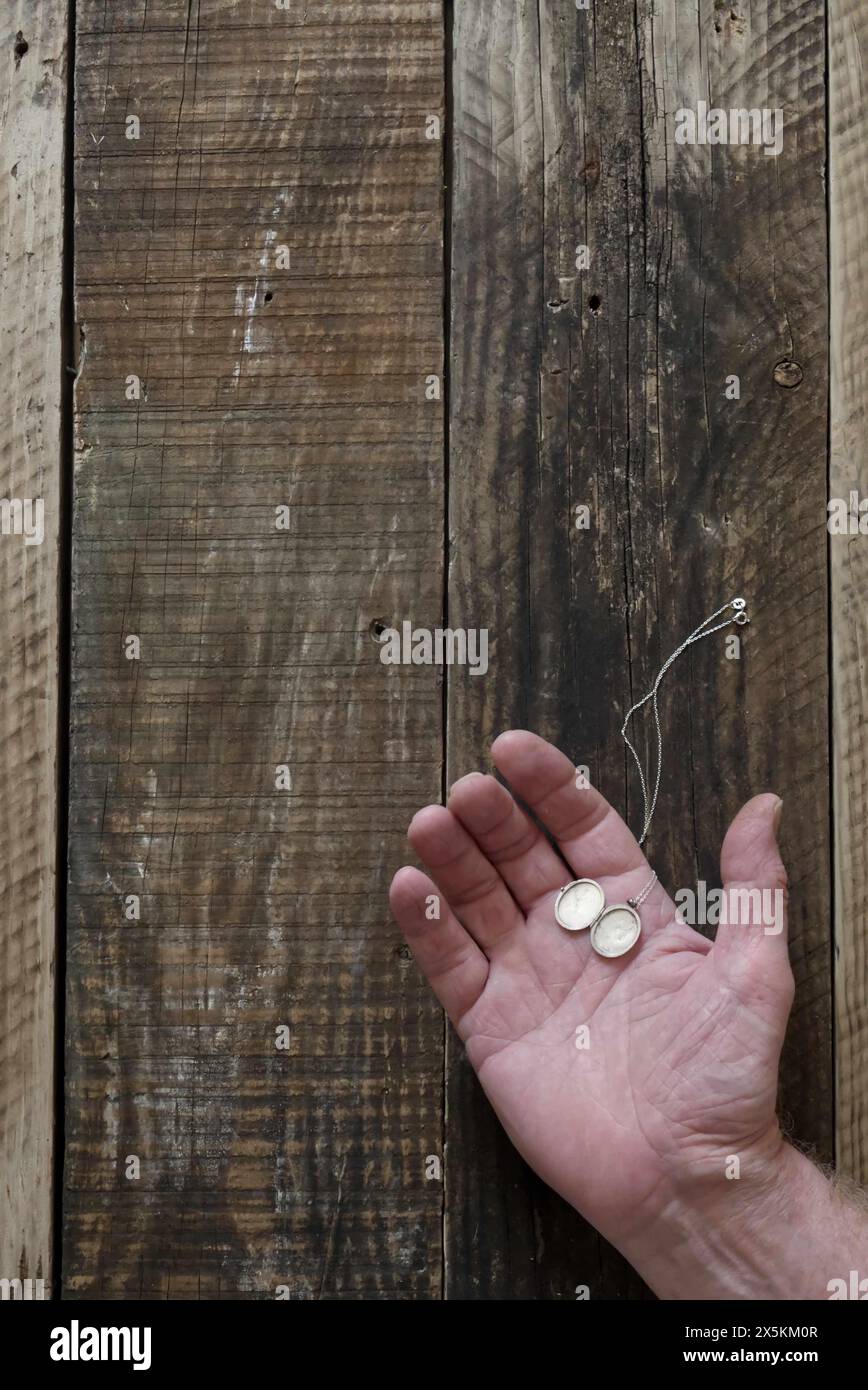 A mans open hand laying on old wood background with silver locket ...