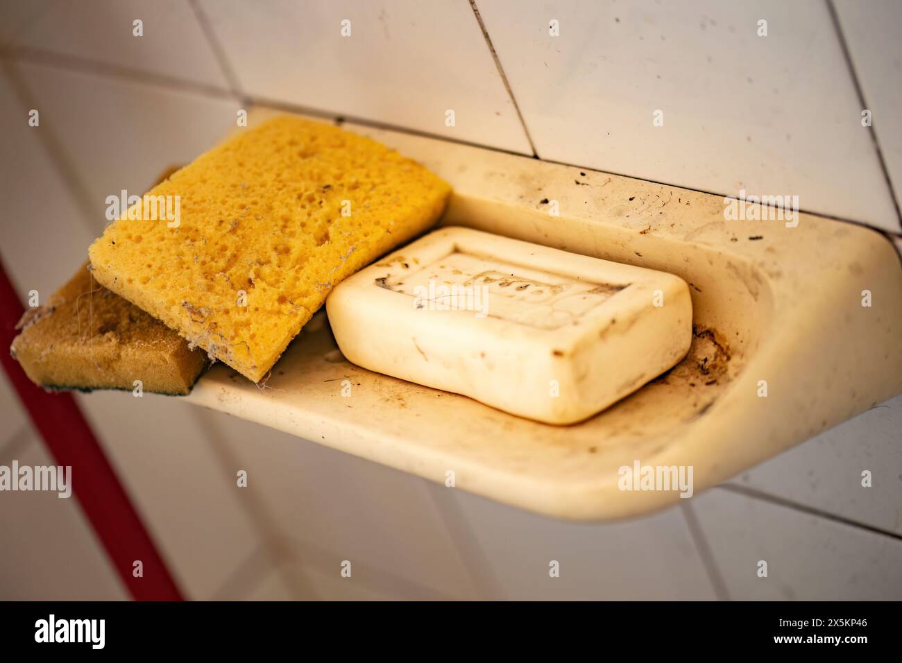 A worn and dirty soap dish holding a bar of soap and a sponge in a ...