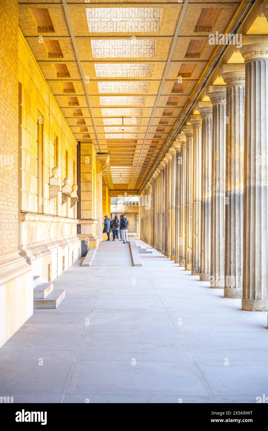 A warm sunlight bathes an elegant colonnade with visitors walking ...
